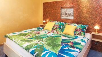 Cama com colcha florida, dois travesseiros amarelos e duas luminárias de cabeceira.
