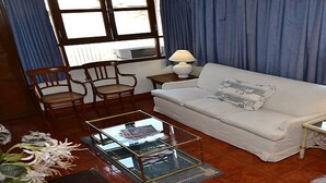 Sala de estar com sofá branco, duas cadeiras de madeira, mesa de centro de vidro e duas mesas laterais com luminárias.