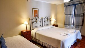 Quarto com duas camas, piso de madeira, luminária no teto e janela com cortinas.