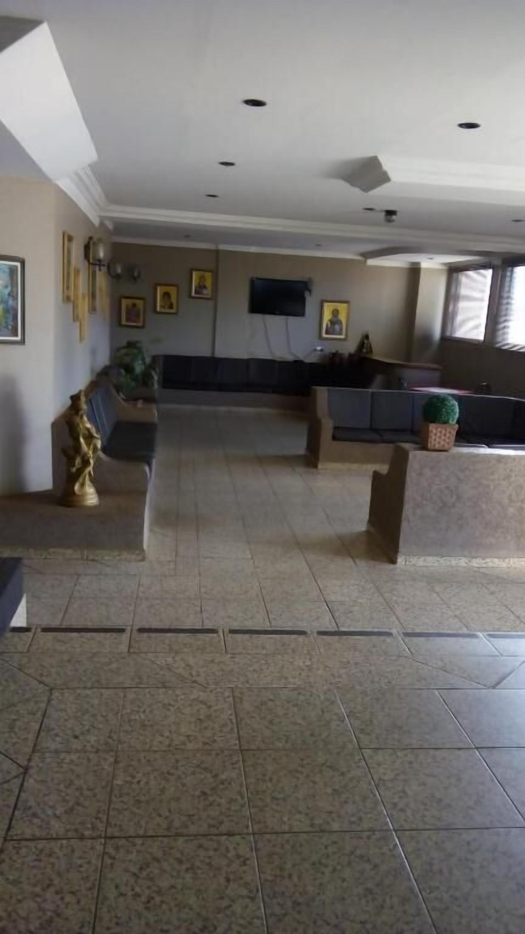 Um hall amplo com área de estar, uma TV de tela plana na parede e um pequeno vaso de planta sobre uma mesa.
