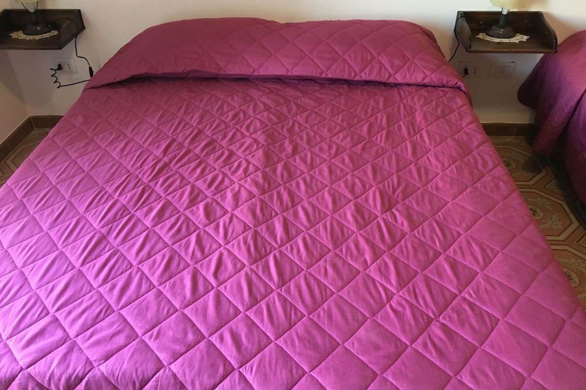 Uma cama com colcha rosa acolchoada e almofadas combinando.
