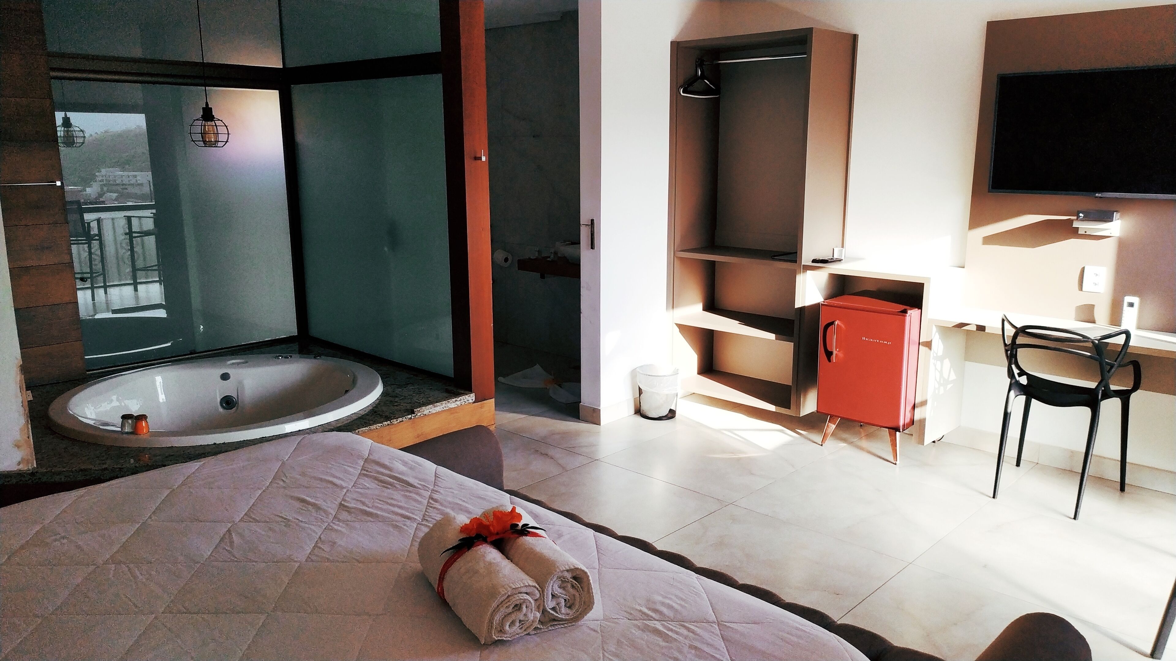 Quarto de hotel moderno com uma cama grande, banheiro com banheira, escrivaninha e televisão.