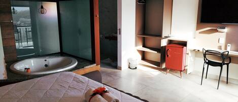 Quarto de hotel moderno com uma cama grande, banheiro com banheira, escrivaninha e televisão.