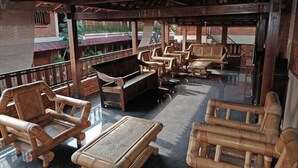 Uma área de estar coberta ao ar livre, com mobiliário de bambu e um piano.