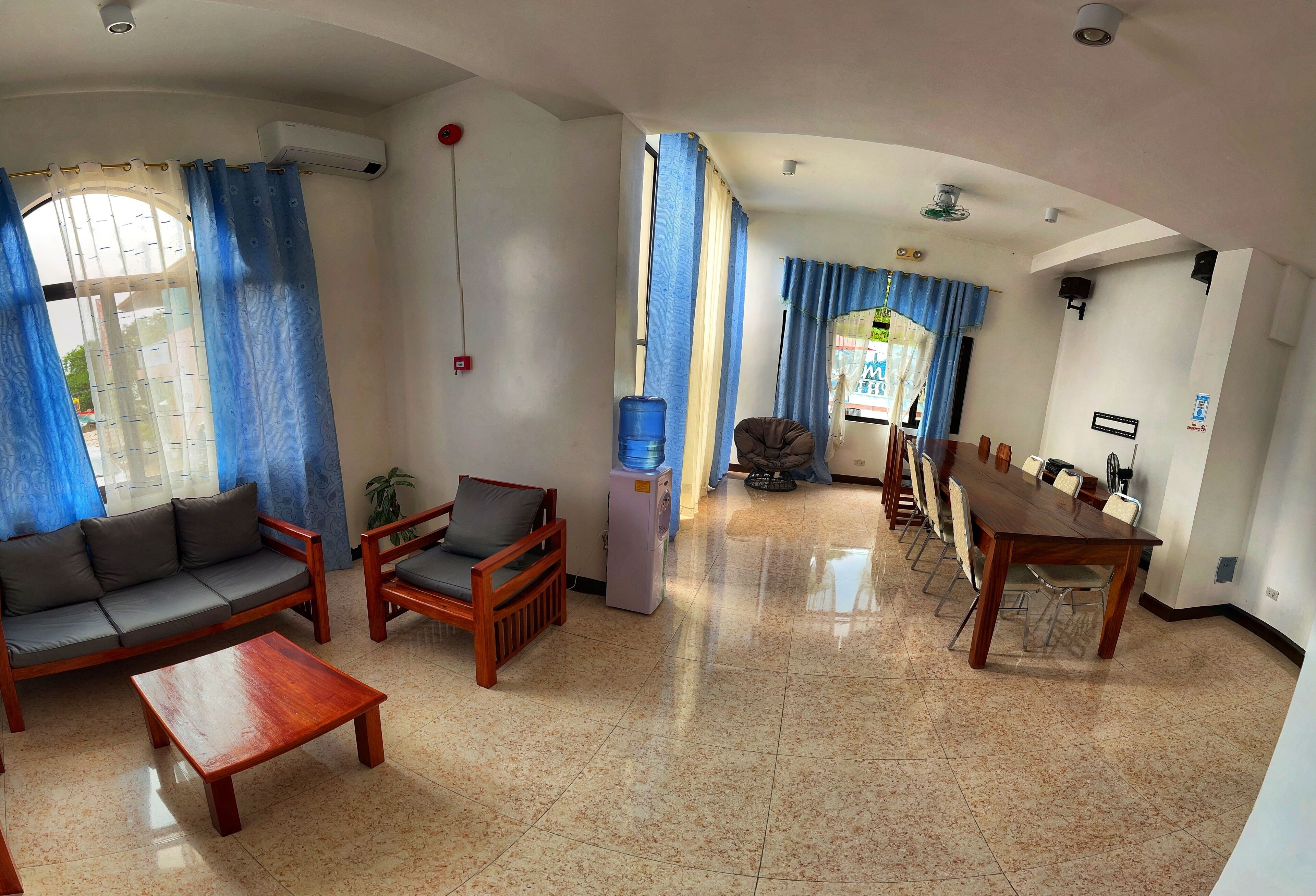Um hall amplo com sofá, cadeiras, mesa de centro, mesa de jantar com cadeiras, dispensador de água e um reservatório de água grande.