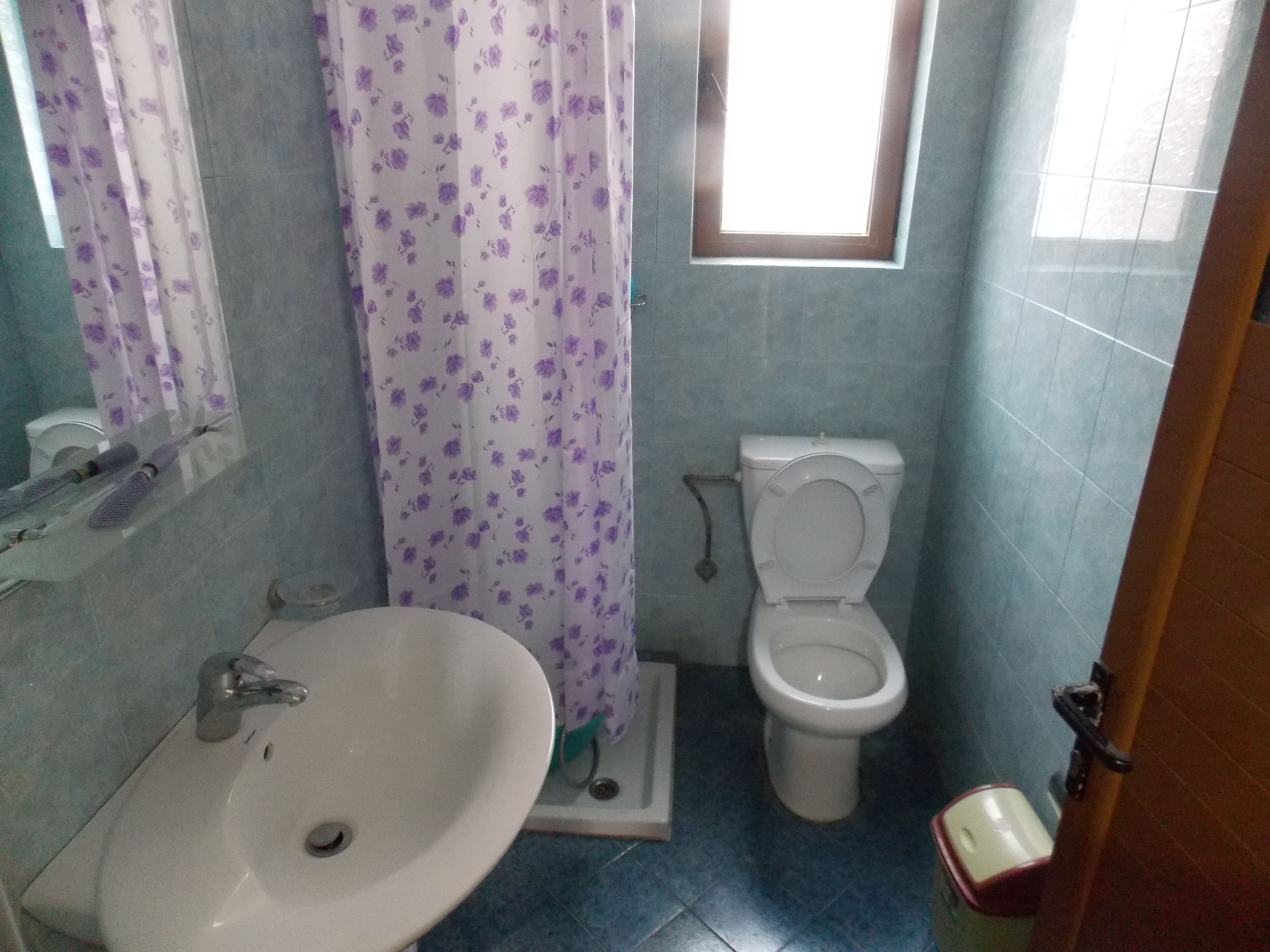 Uma casa de banho com lavatório branco, sanita e cortina de chuveiro com padrão floral roxo.