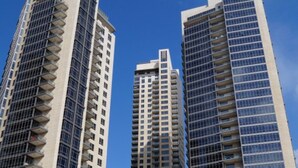 Um edifício moderno e imponente com fachada de vidro, rodeado por palmeiras e um céu claro.