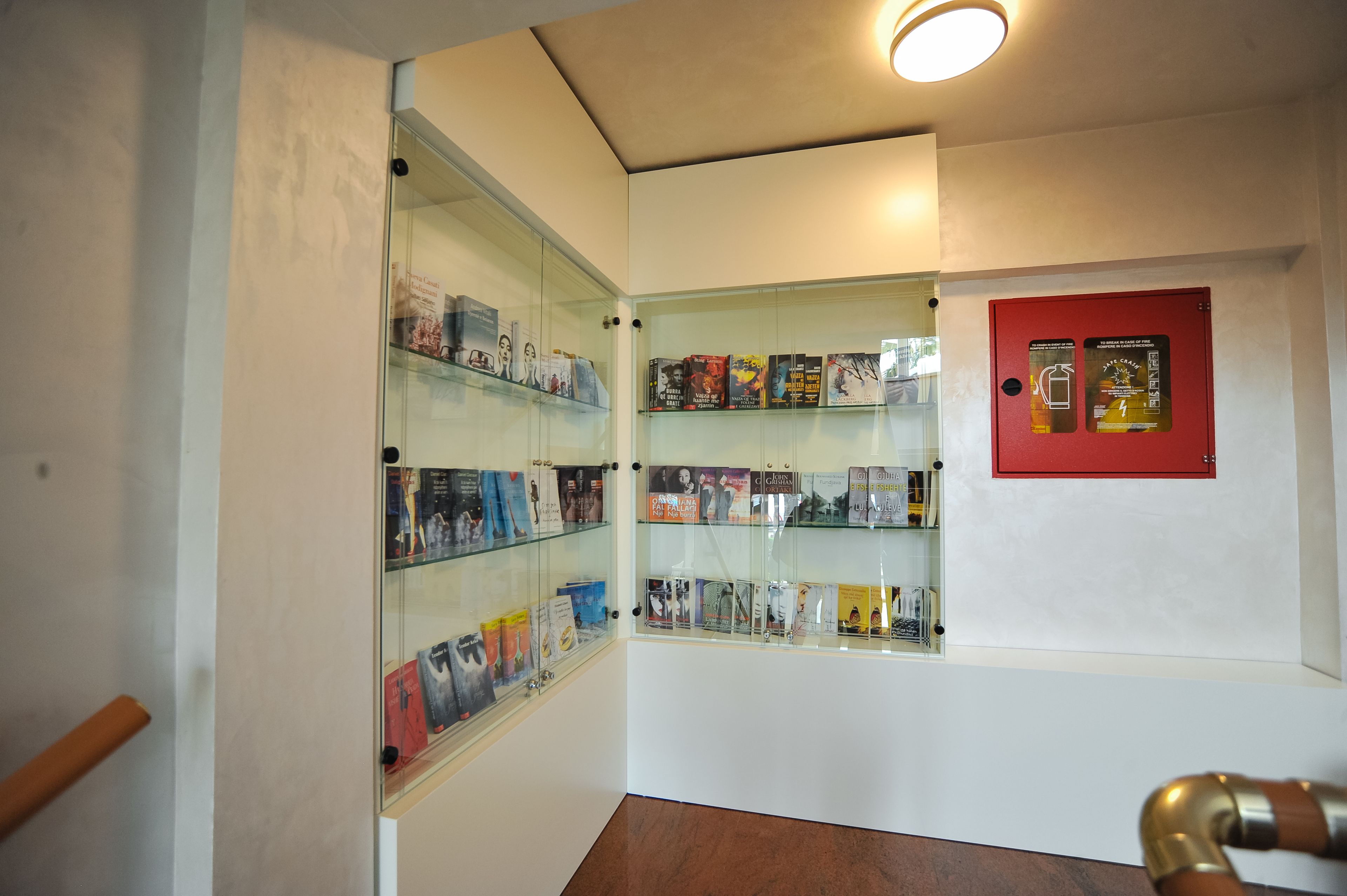 Corredor com vitrines de vidro contendo livros e um cartaz de segurança contra incêndio na parede.