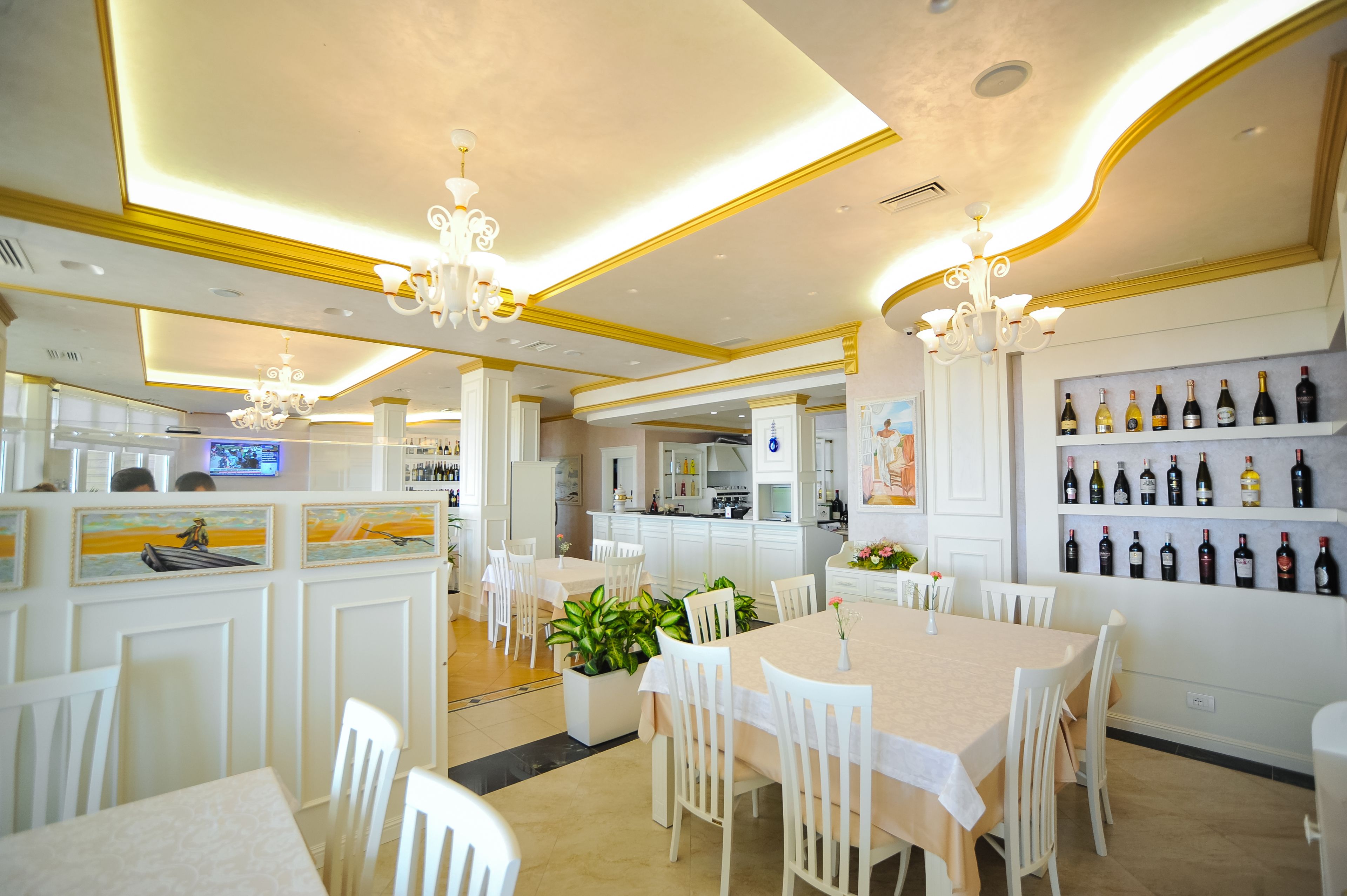 Um restaurante com mobiliário branco, um candelabro e uma parede de vinhos.