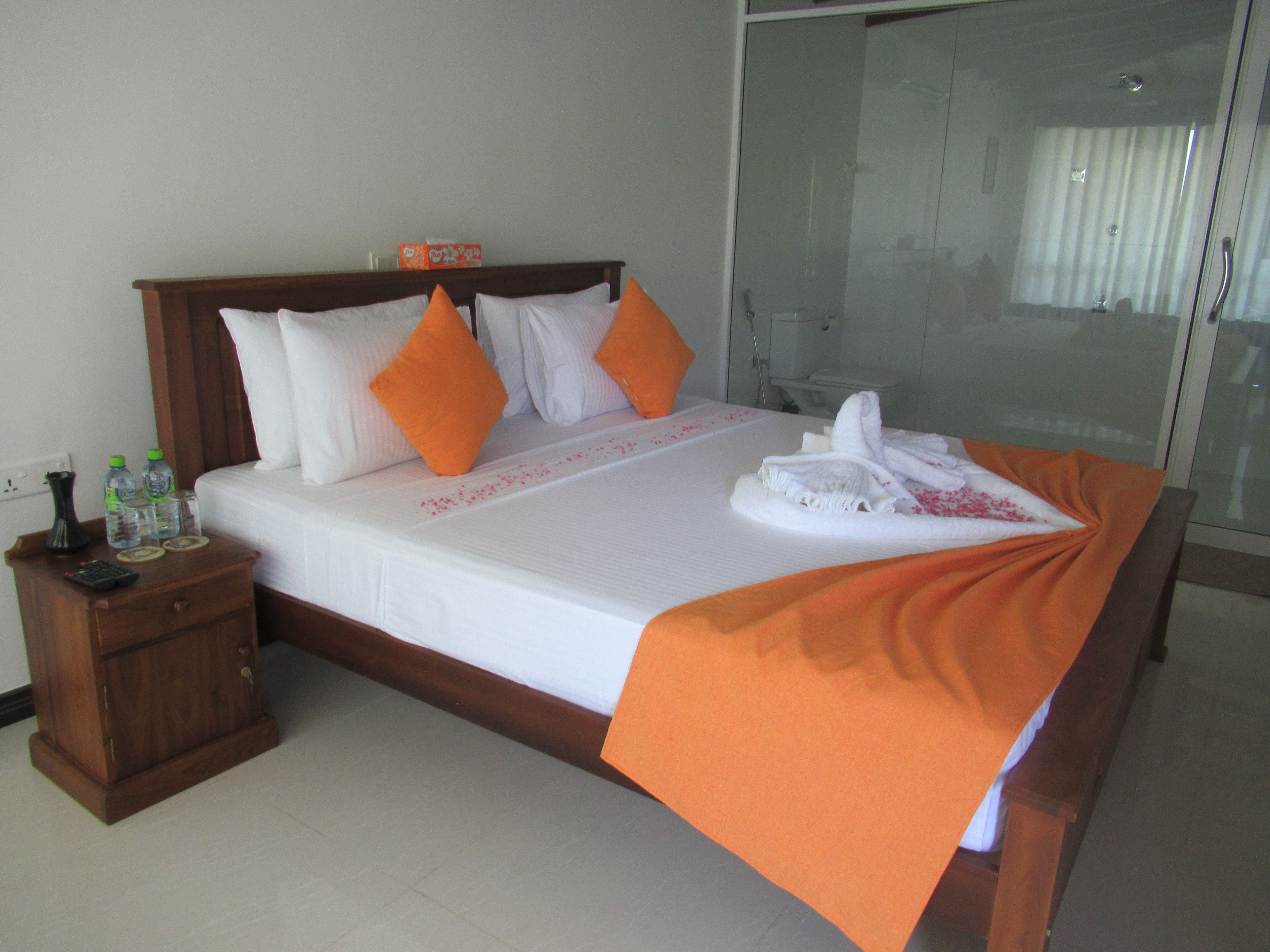 Quarto de hotel com uma cama, mesa de cabeceira, cabine de chuveiro de vidro e banheiro visível através da porta de vidro.