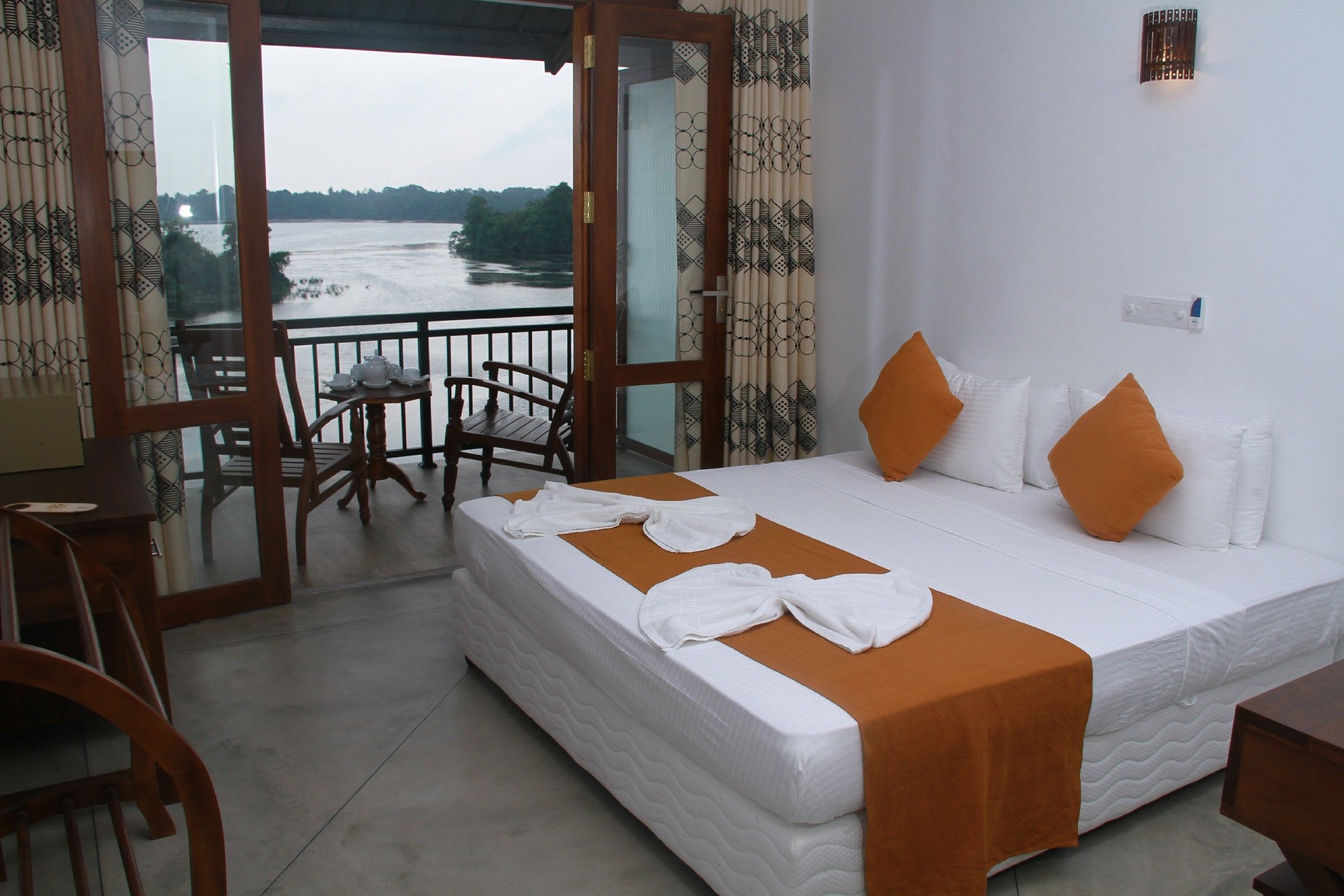 Quarto de hotel com uma cama grande, almofadas laranja, uma cadeira de madeira e uma mesa.