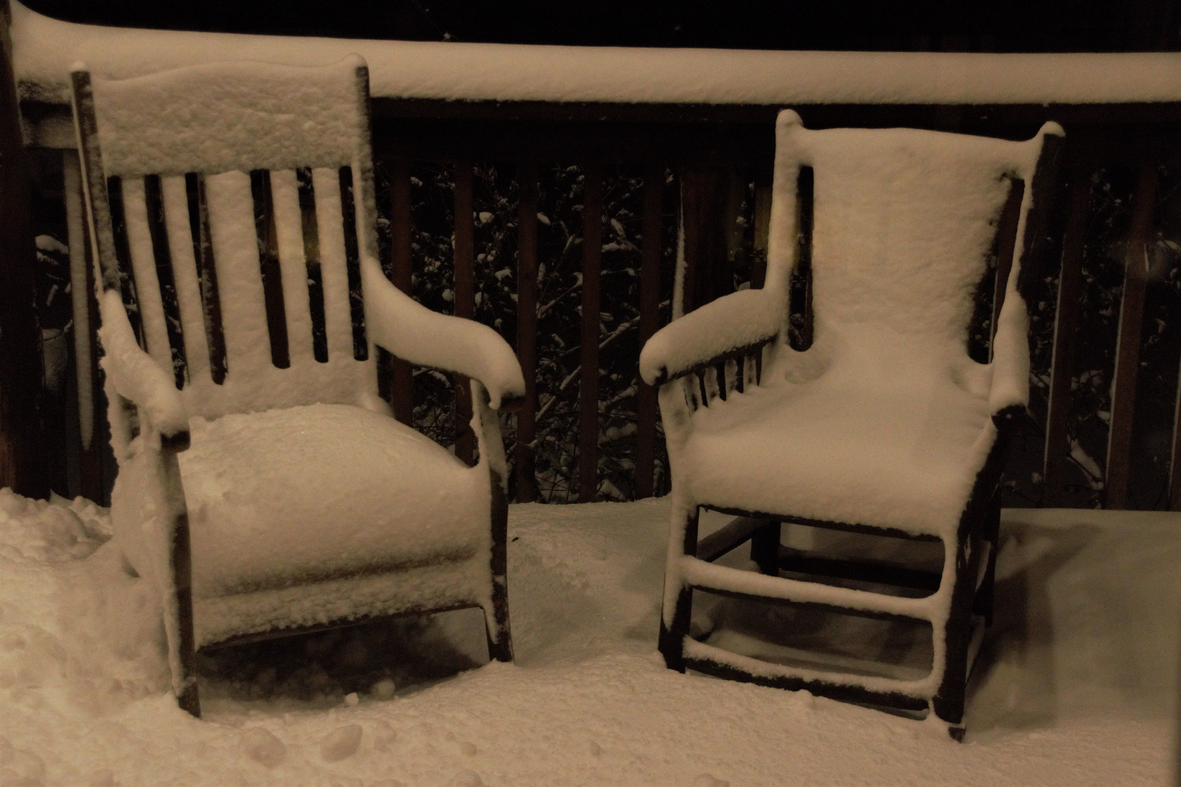 Duas cadeiras cobertas de neve em frente a uma cerca de madeira.
