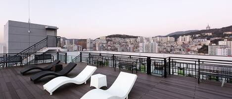 Um lounge no terraço com espreguiçadeiras brancas e vista para a cidade.