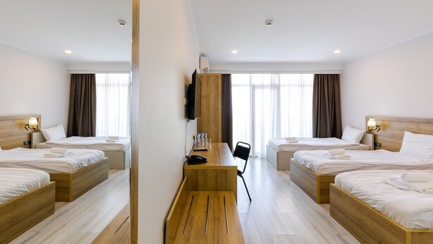 Quarto de hotel com duas camas, uma escrivaninha de madeira, televisão de tela plana e uma janela grande com cortinas.
