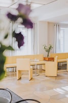 Um saguão de hotel com um sofá amarelo, uma mesinha e um vaso com plantas.