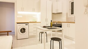 Cozinha moderna com armários brancos, máquina de lavar embutida e área de refeições com banquetas.