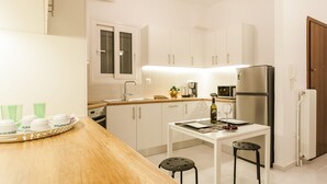Uma cozinha moderna com armários brancos, uma geladeira de aço inoxidável, bancada de madeira e uma pequena mesa de jantar com banquetas.
