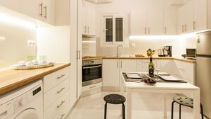 Uma cozinha moderna com armários brancos, bancada de madeira, forno embutido, pia e um espaço de refeições com banquetas.