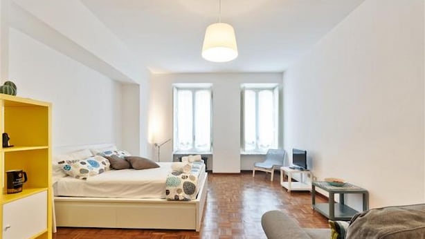 Quarto com cama, estante amarela, escrivaninha, cadeira e televisão.