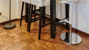 Cozinha moderna com bancada escura, cadeiras brancas e um abajur alto.
