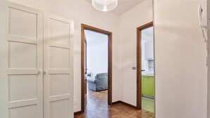 Um corredor com piso de madeira, paredes brancas e uma porta que dá para uma sala de estar com um sofá.