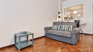 Sala de estar com sofá cinzento, mesa lateral azul e chão de madeira em padrão herringbone.