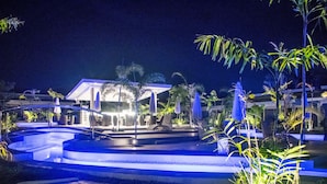 Área de piscina de um resort à noite, com um lounge bem iluminado e espaço para sentar.