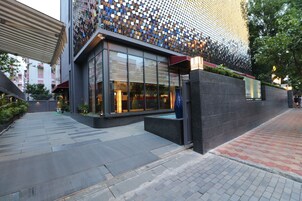 Um edifício moderno com fachada em mosaico única, janelas amplas e área externa bem cuidada com caminho e floreiras.