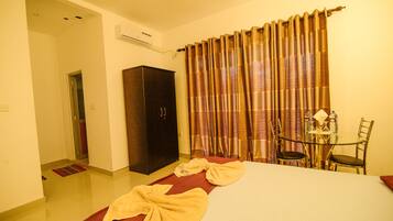 Quarto de hotel com cama, guarda-roupa, mesa e cadeiras, e cortina.