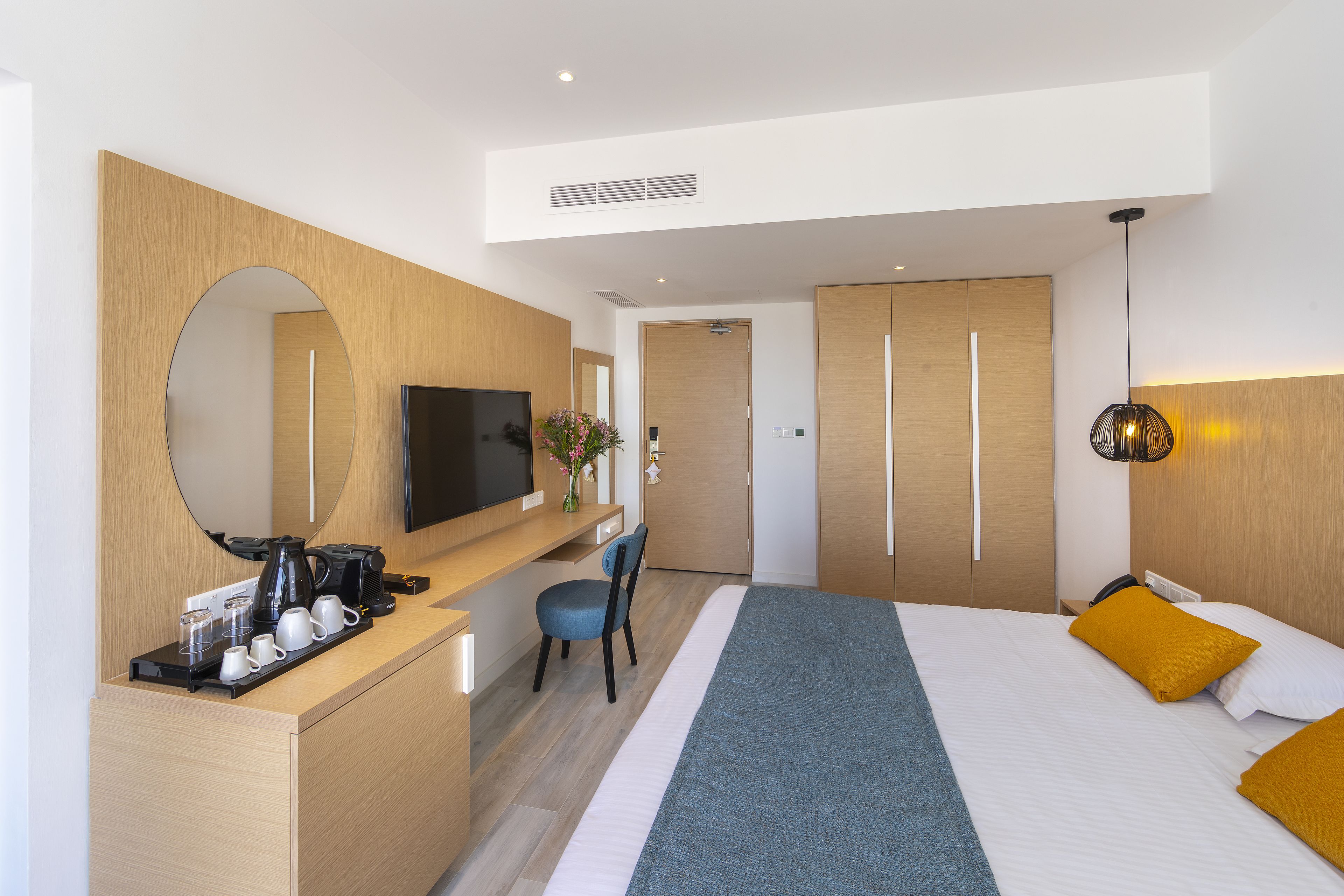 Quarto de hotel moderno com cama, escrivaninha com máquina de café, televisão e espelho.