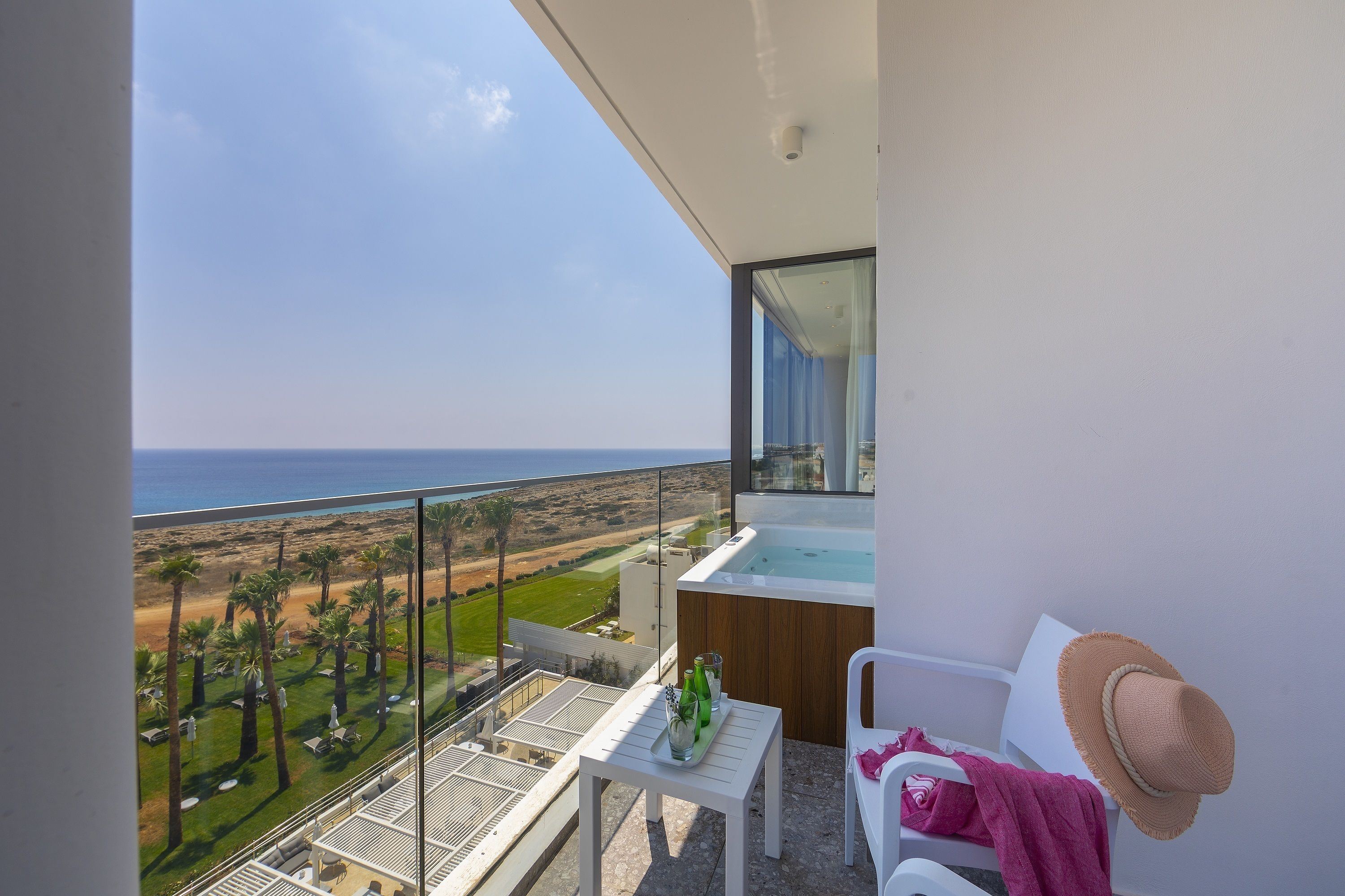 Uma varanda com vista para a praia, uma banheira de hidromassagem e uma mesa com garrafas.