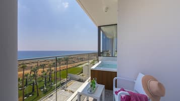 Uma varanda com vista para a praia, uma banheira de hidromassagem e uma mesa com garrafas.