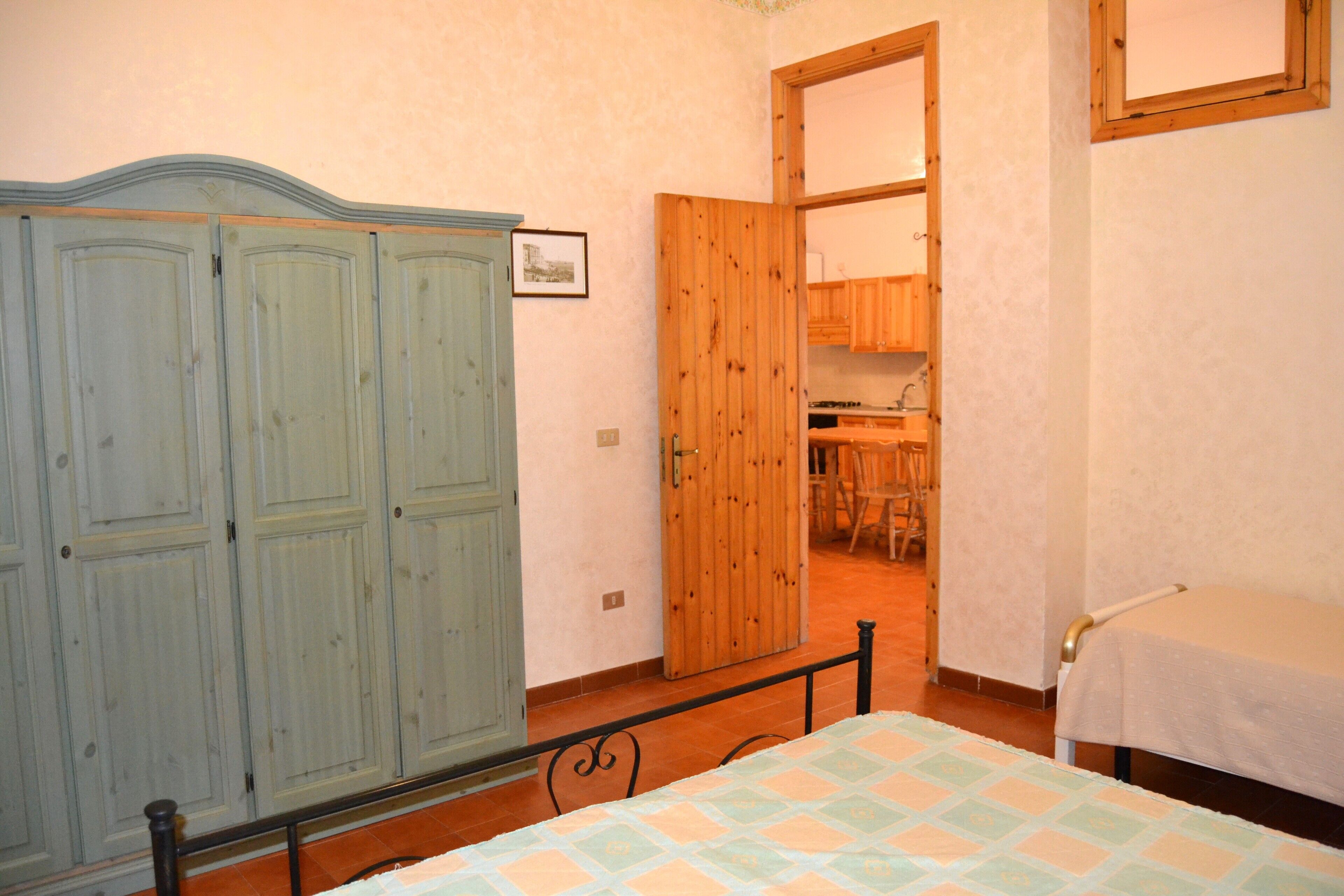 Quarto com cama, guarda-roupa e vista para a cozinha.