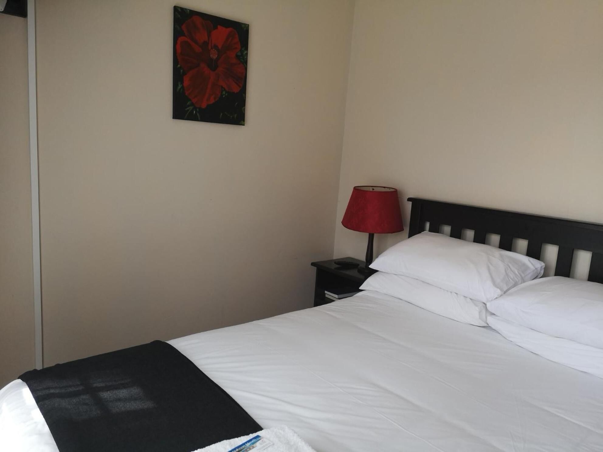 Uma cama bem arrumada com lençóis brancos, uma cabeceira preta e um abajur vermelho em uma mesinha de cabeceira.