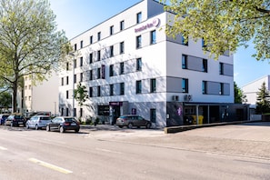 Um hotel moderno com fachada plana, várias janelas e um estacionamento com diversos carros.