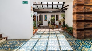 Um corredor com ladrilhos estampados, plantas em vasos e uma estrutura de parede de madeira.