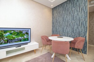 Uma sala de estar moderna com televisão de tela plana, um rack branco, uma mesa redonda branca e cadeiras cor-de-rosa.