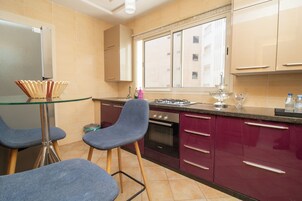 Cozinha moderna com mesa de jantar de vidro, duas cadeiras azuis, geladeira de aço inoxidável, fogão a gás e armários vinho.