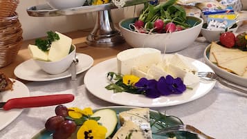 Uma mesa de buffet com diversos queijos, frutas e uma saladeira.