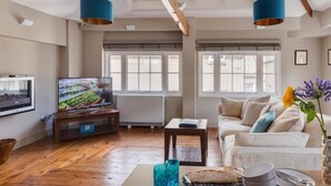 Uma sala de estar aconchegante com piso de madeira, uma televisão, um sofá branco e uma mesa de centro.