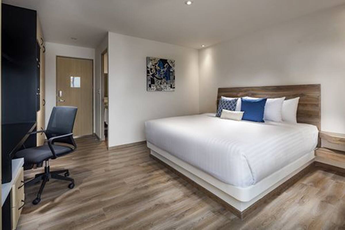 Quarto de hotel com uma cama grande, uma escrivaninha com cadeira e piso de madeira.
