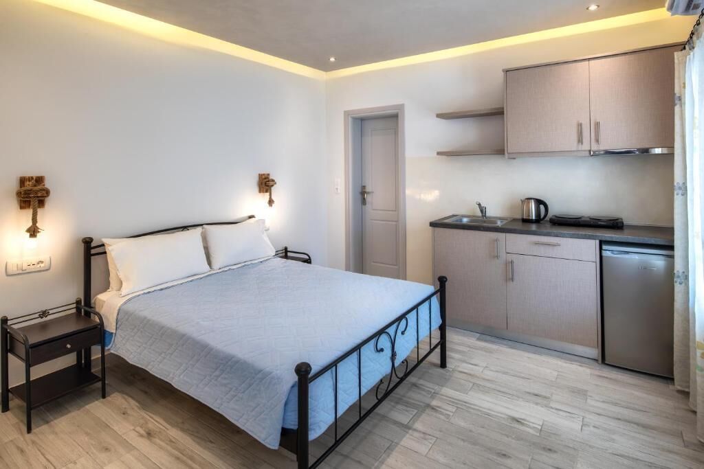 Quarto compacto com cama, mesa de cabeceira e uma pequena cozinha compacta com pia e armários.