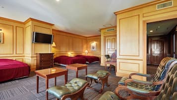 Quarto de hotel com uma cama grande, uma mesa de escritório, duas poltronas, uma televisão e uma porta que dá para outro quarto.
