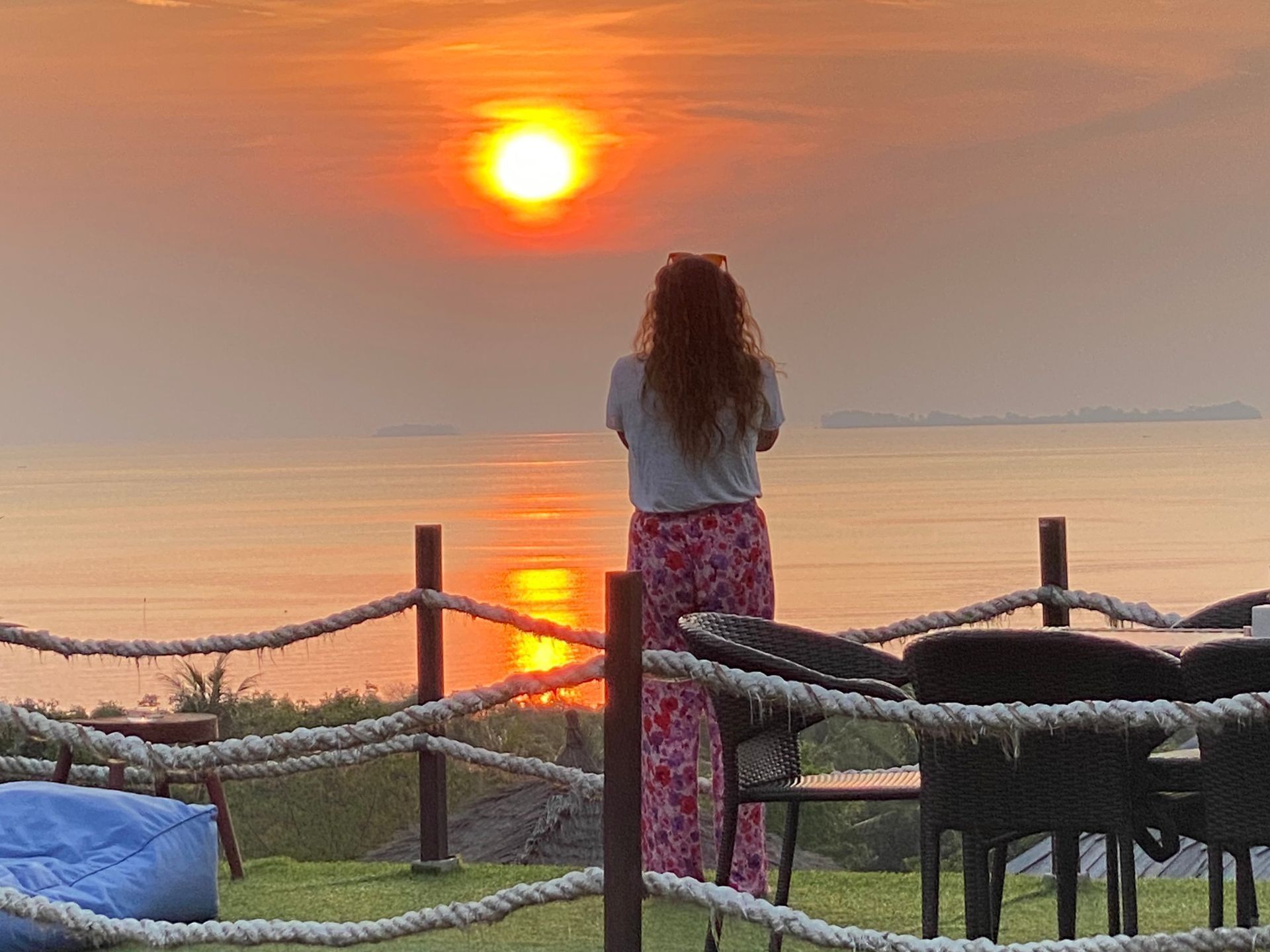 Uma pessoa parada perto de uma barreira de corda, apreciando a vista da água ao pôr do sol.