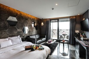 Quarto de hotel moderno com uma cama grande, um sofá, uma área de refeições e uma televisão.