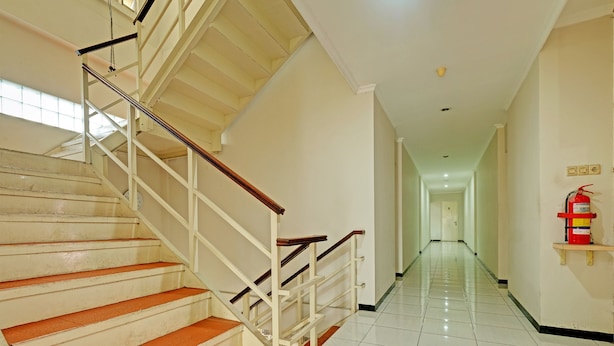 Um corredor de hotel com escadas, um extintor de incêndio e um chão limpo revestido de azulejos.
