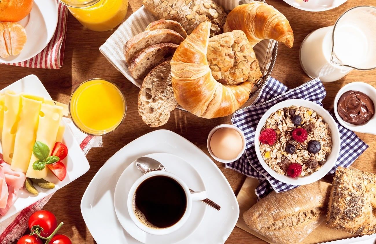 Uma mesa de café da manhã com croissants, pão, queijo, tomates e uma tigela de cereal com frutas vermelhas.