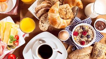 Uma mesa de café da manhã com croissants, pão, queijo, tomates e uma tigela de cereal com frutas vermelhas.