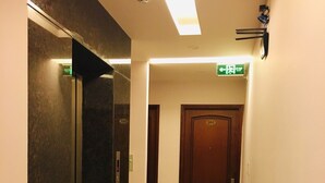 Corredor de hotel com piso de mármore, porta de madeira com a inscrição '203' e sinal de saída de emergência.