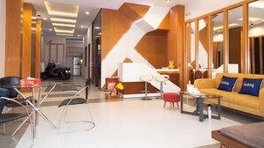 Um lobby de hotel moderno com balcão de recepção, área de estar e uma motocicleta estacionada ao fundo.